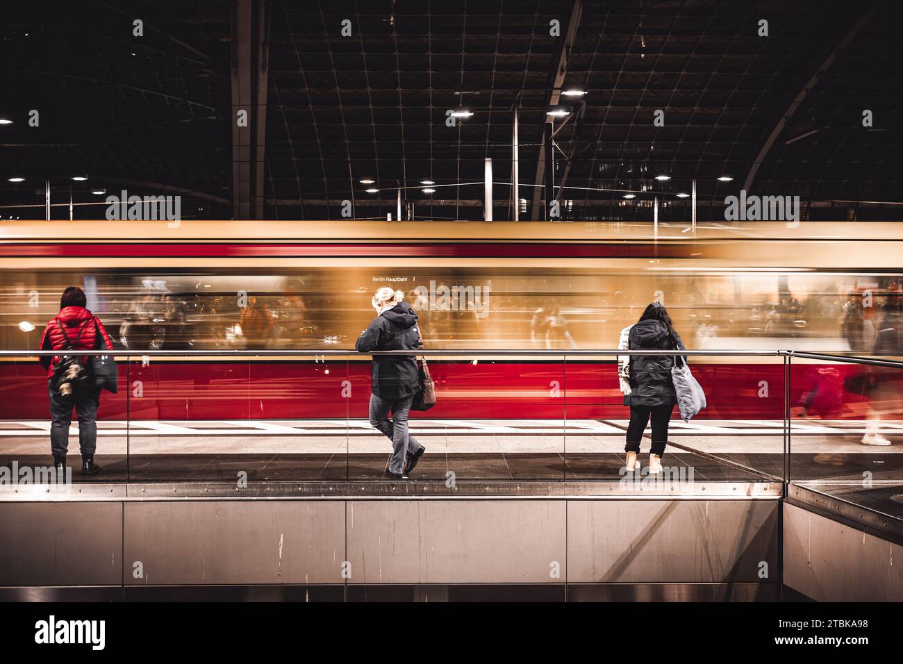 A group of people stand side-by-side at a bustling train station ...