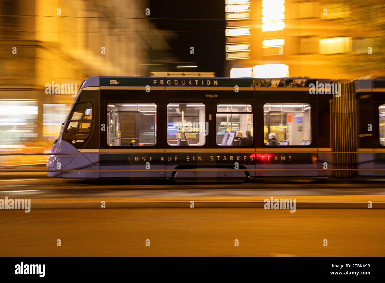 An illuminated tram car is driving along a track in a nighttime setting ...