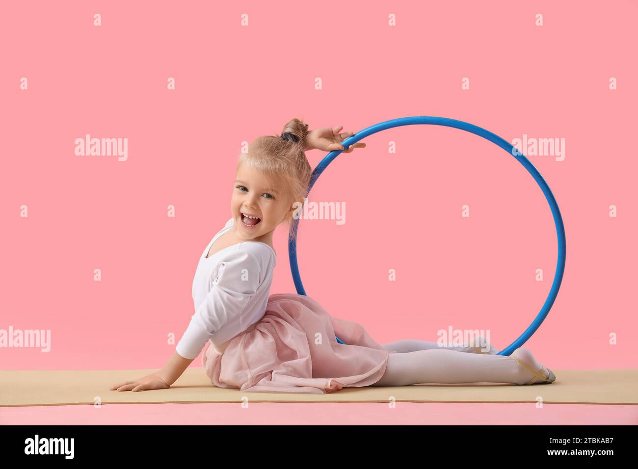 Cute little girl doing gymnastics with hula hoop on mat against pink ...