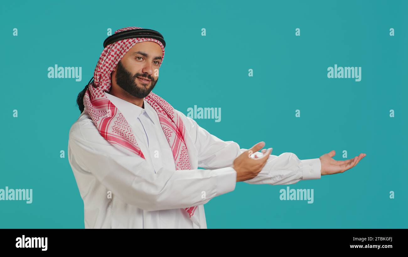 Muslim guy wearing traditional robe and ghutra gesturing to side with ...