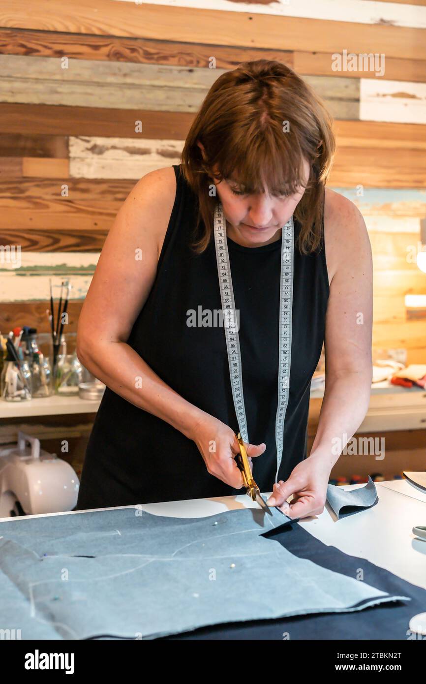 Seamstress using scissors to cut textile at work table. Vertical Shot ...