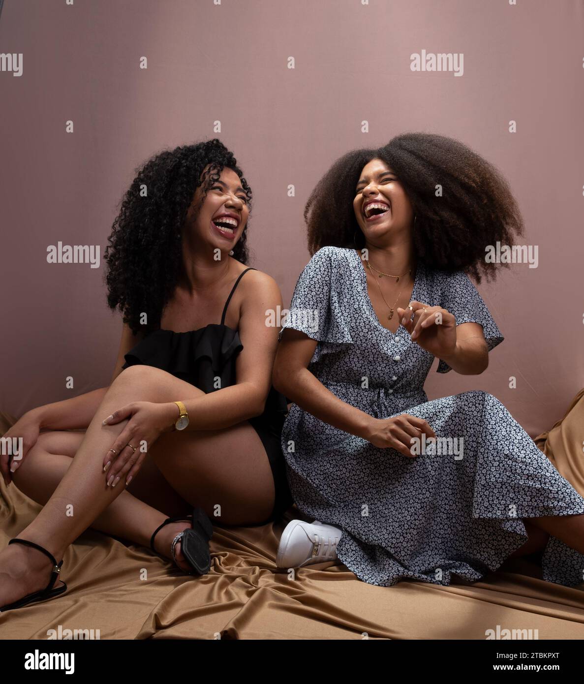 Two young, happy, beautiful friends looking at each other, sitting ...