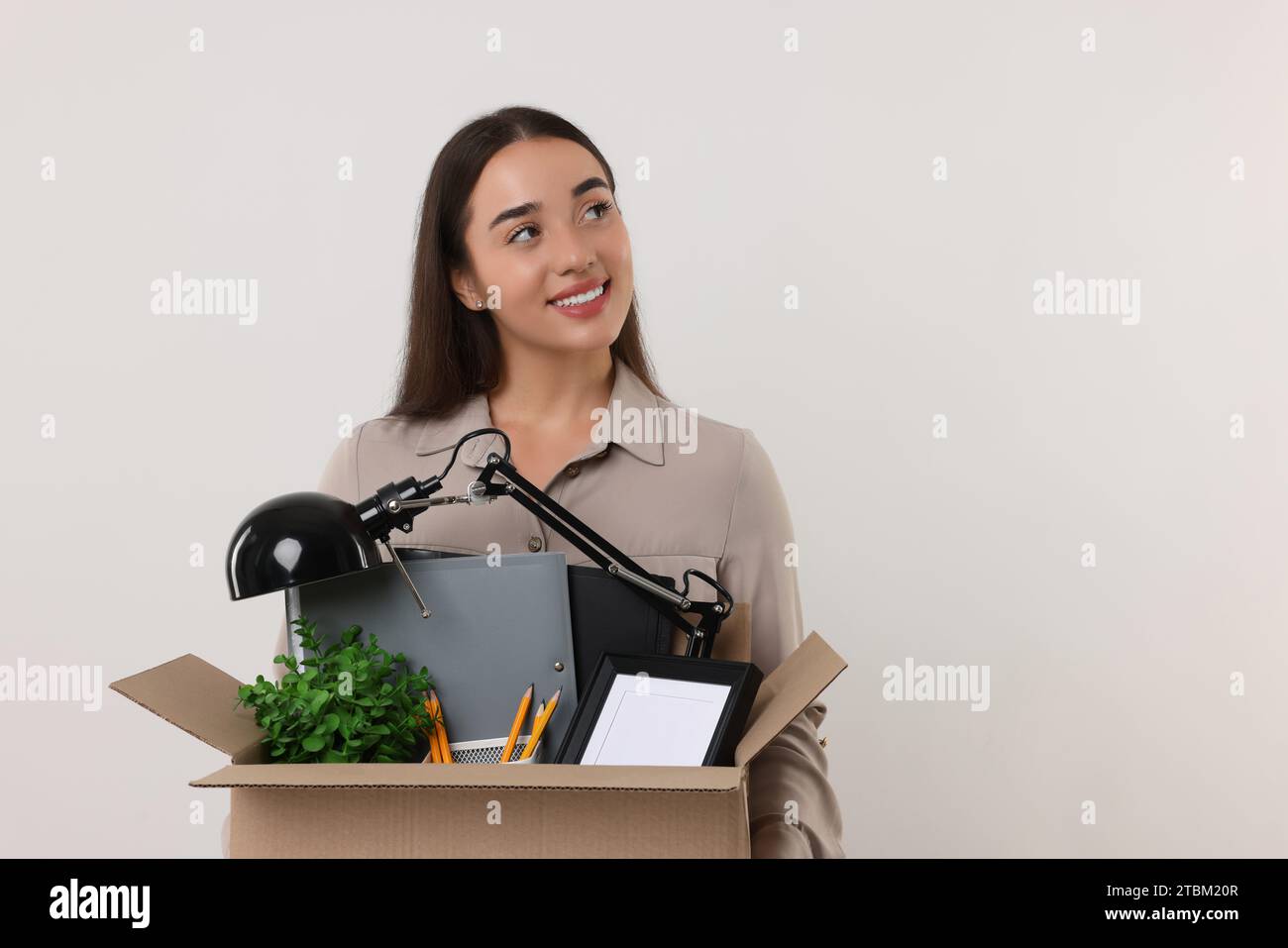 Happy unemployed woman with box of personal office belongings on white ...