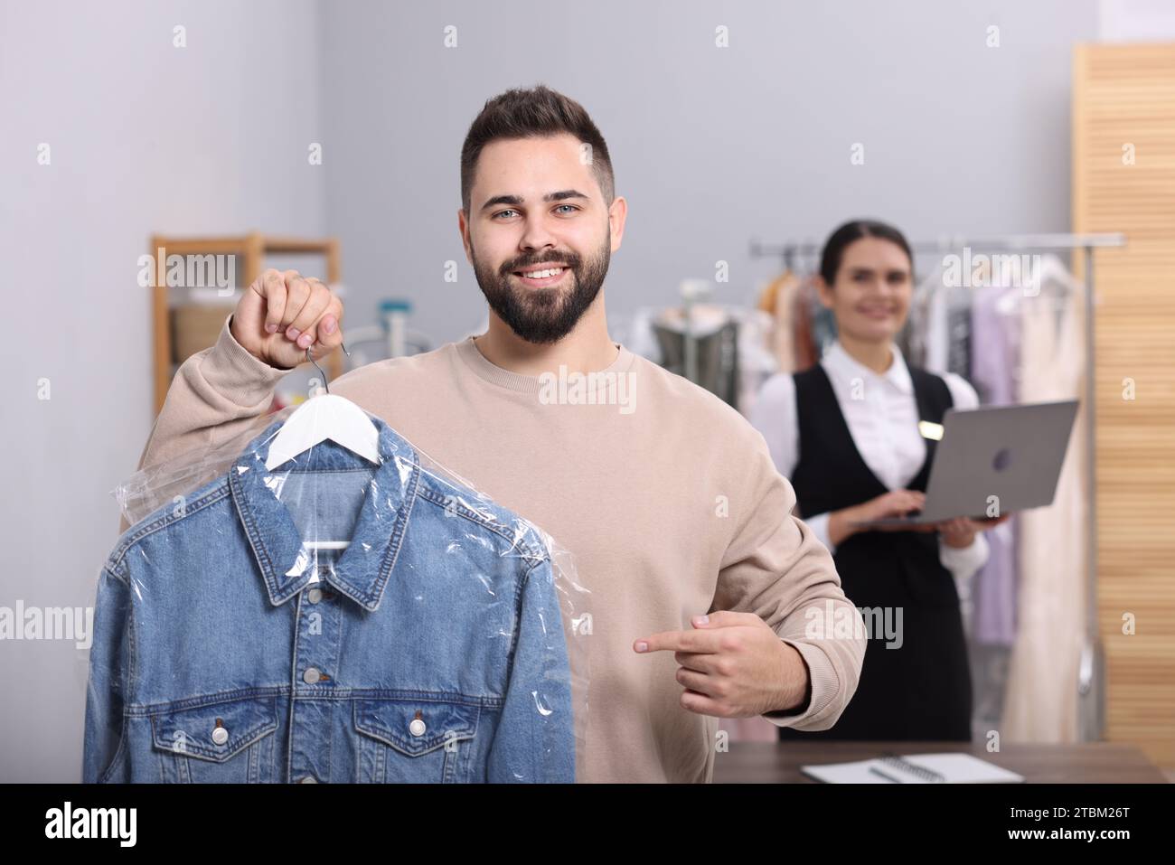 Dry-cleaning service. Happy man holding hanger with denim jacket in ...