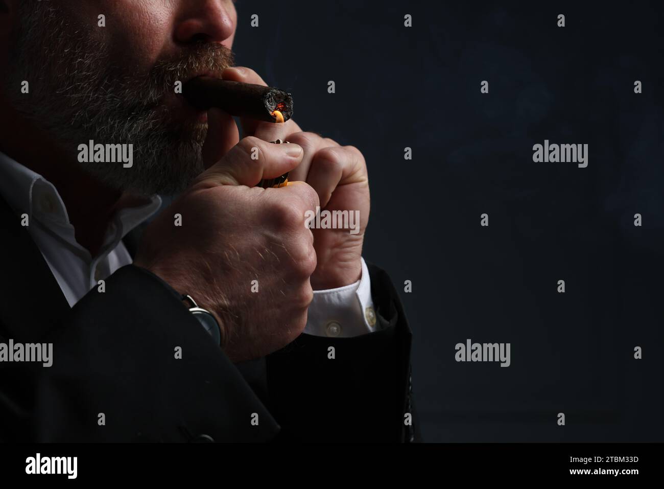 Bearded man lighting cigar on dark grey background, closeup. Space for ...