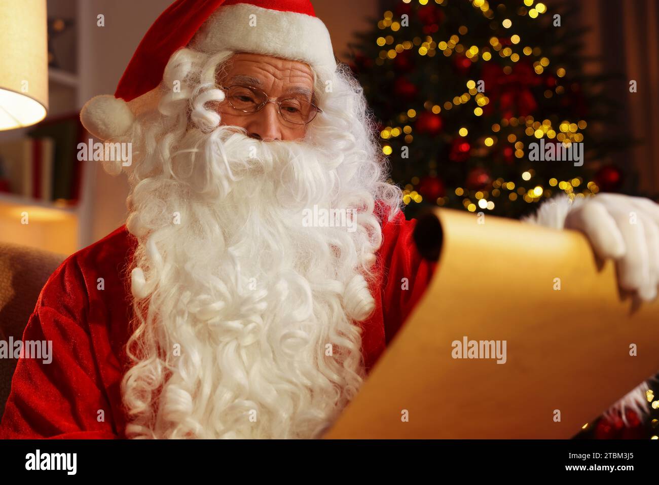 Santa Claus reading letter in room with Christmas tree Stock Photo - Alamy