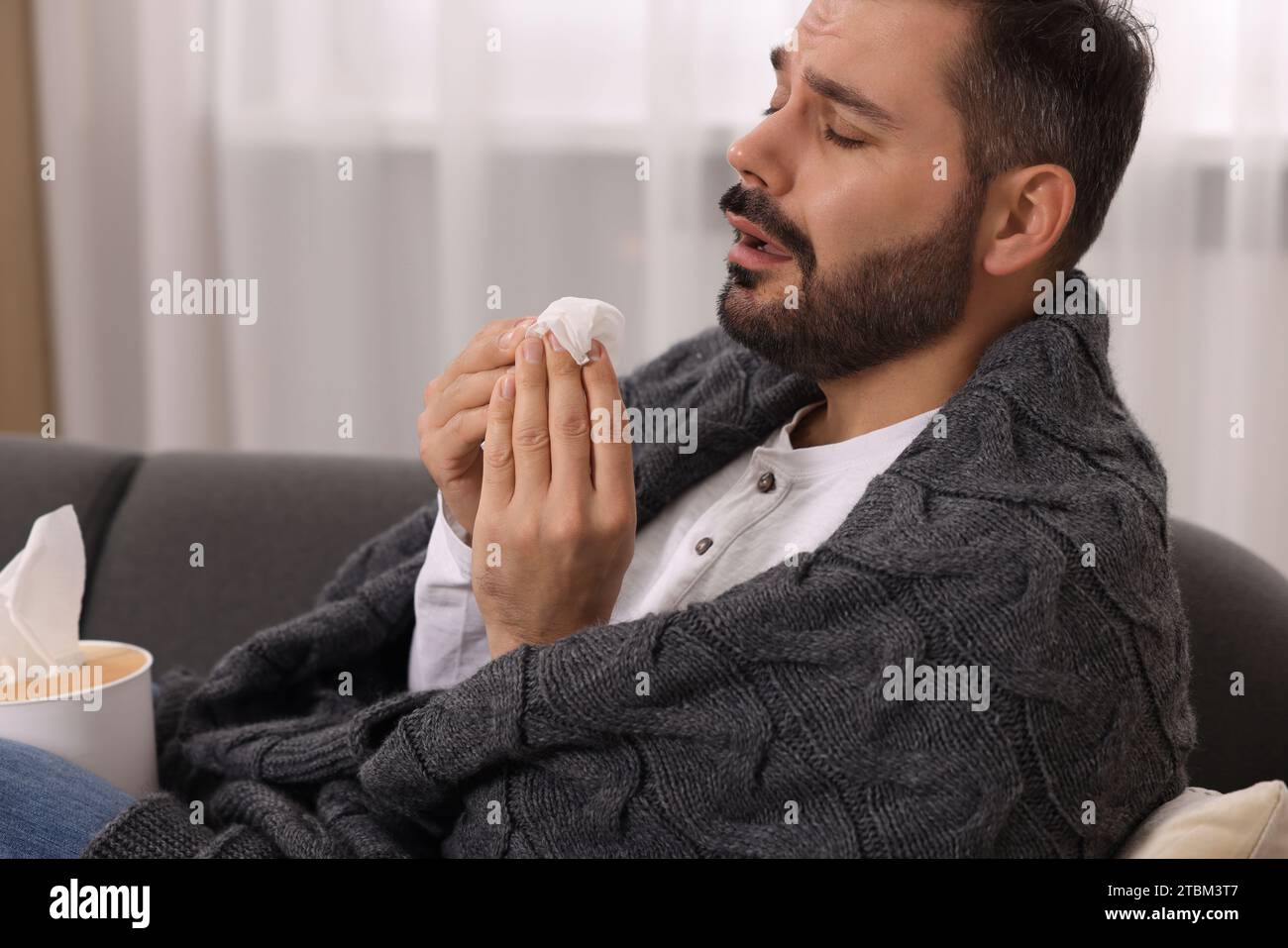 Sick man wrapped in blanket with tissue on sofa at home. Cold symptoms ...