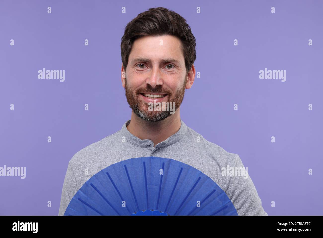Happy man holding hand fan on purple background Stock Photo - Alamy