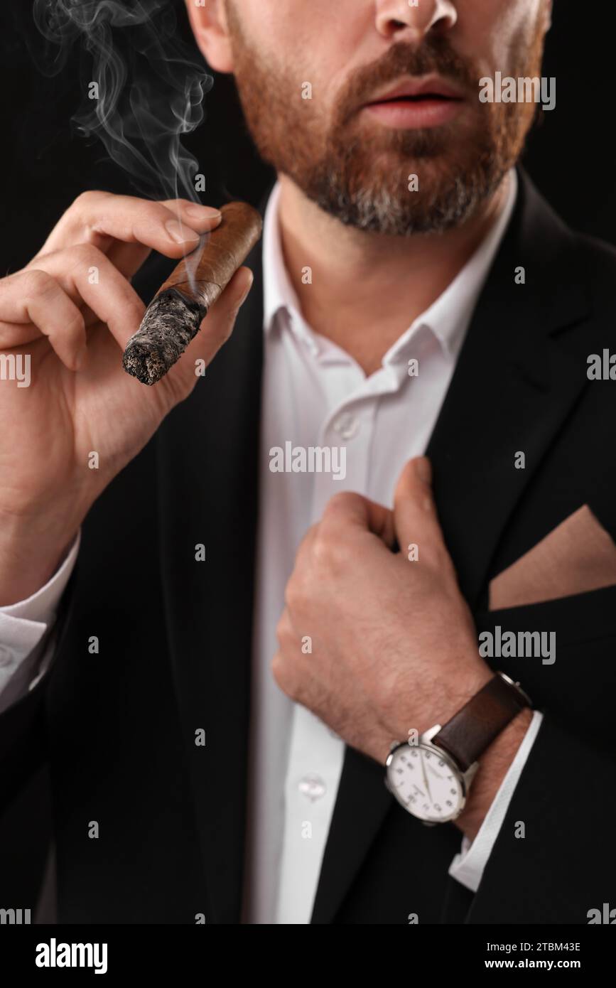 Man in elegant suit smoking cigar on black background, closeup Stock Photo - Alamy