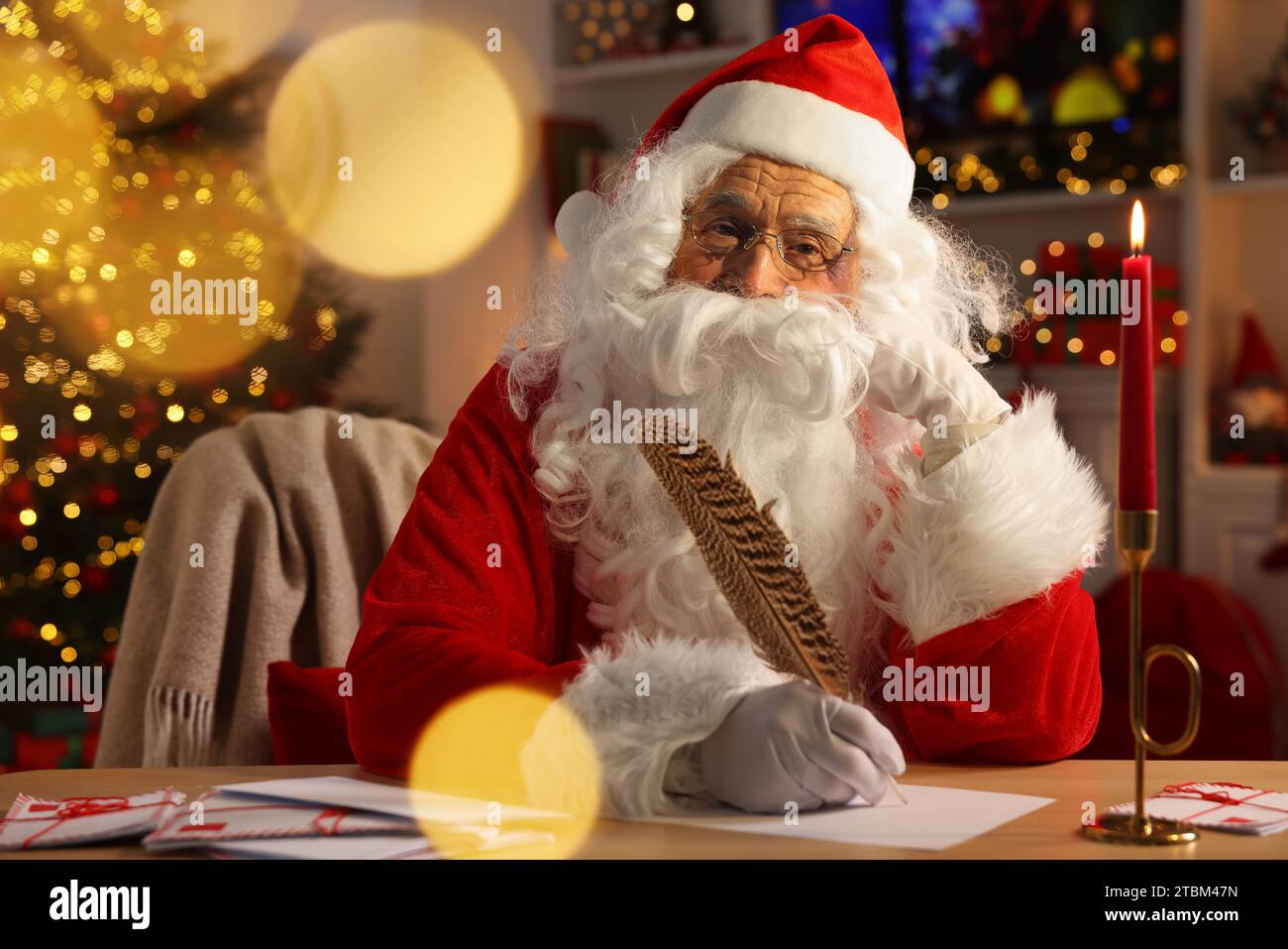 Santa Claus writing letter at table in room decorated for Christmas ...