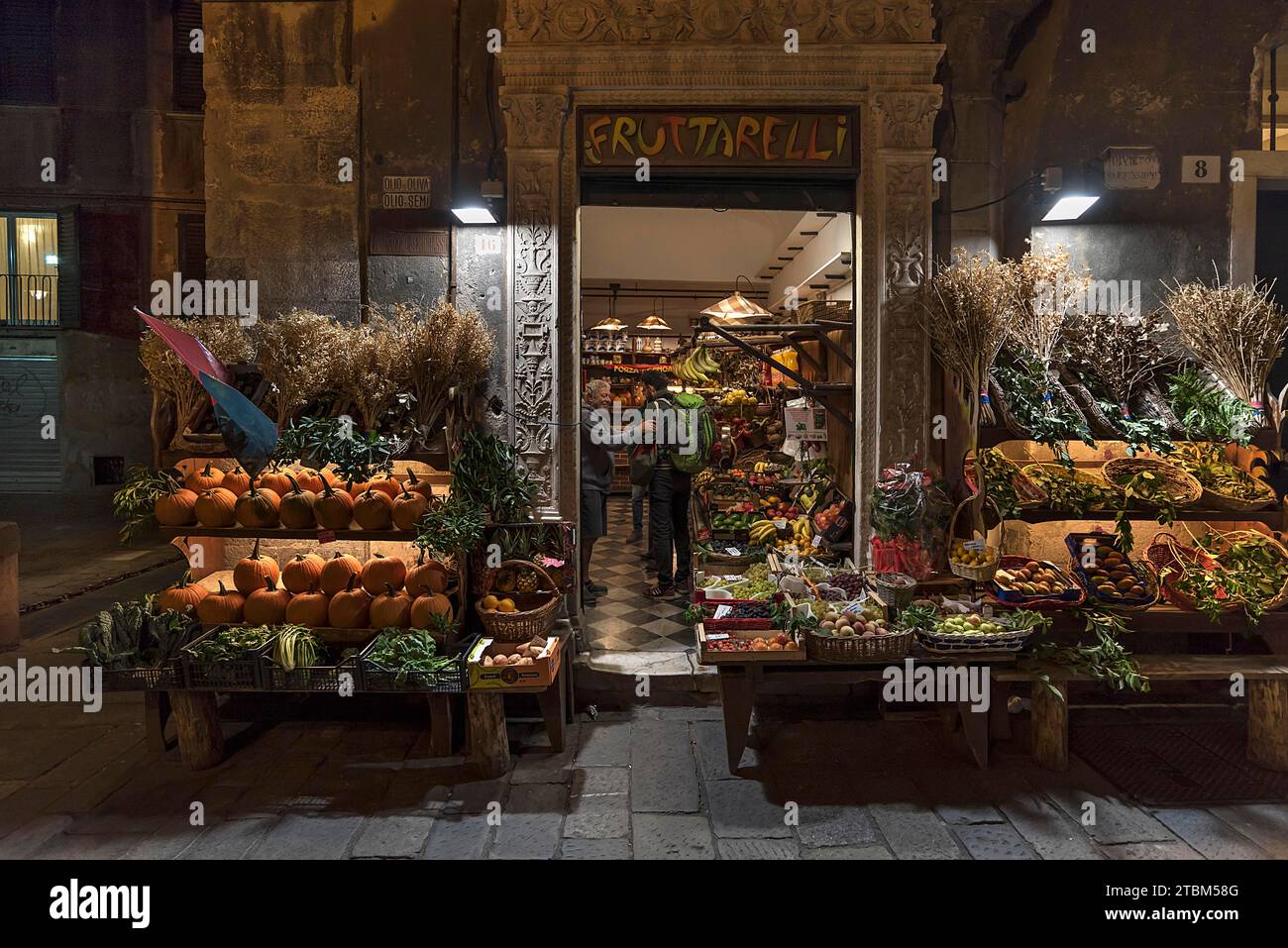 Customers in a fruit shop open at night in the historic centre, Genoa ...