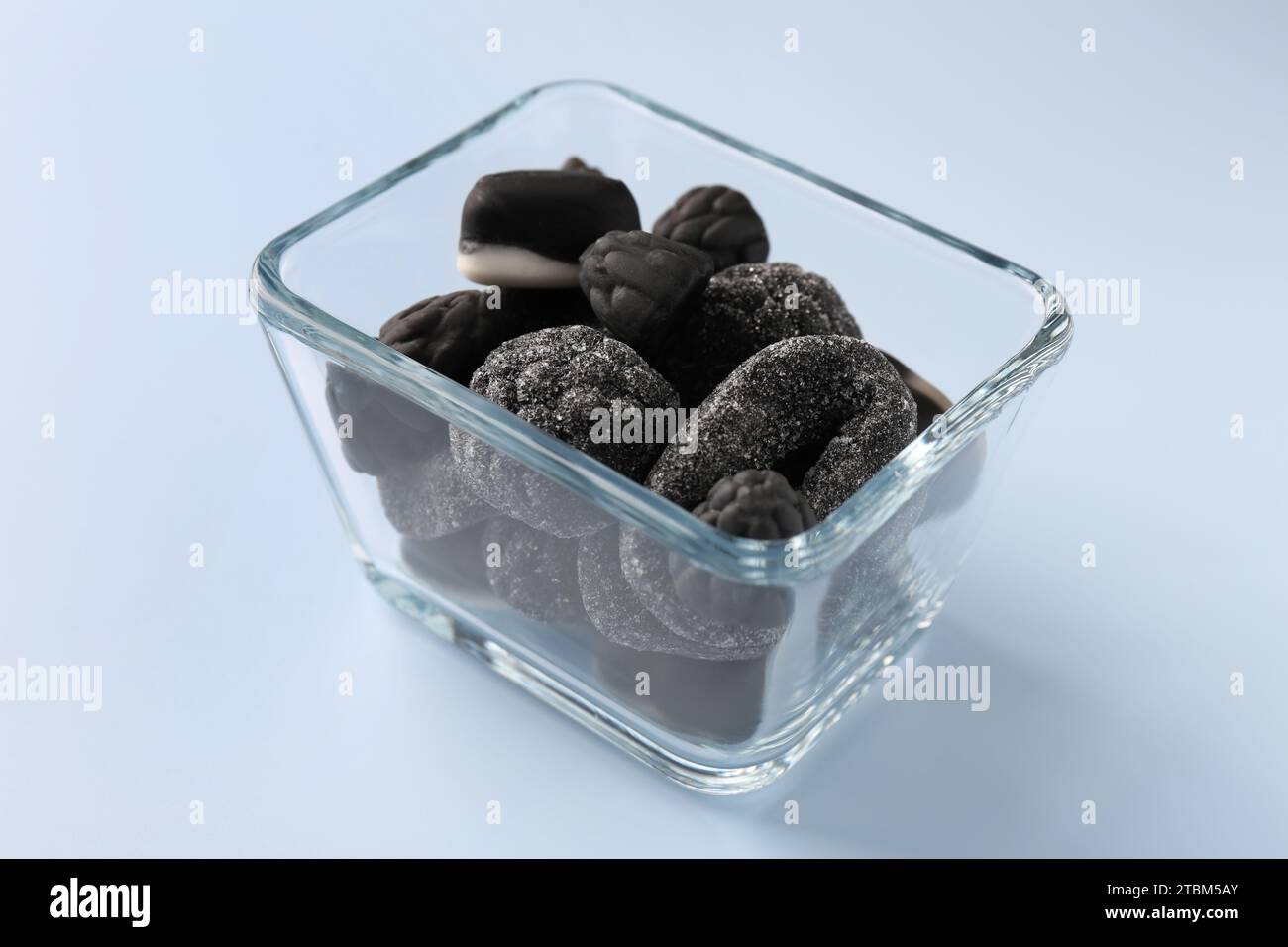 Glass container of tasty liquorice candies on light blue background ...