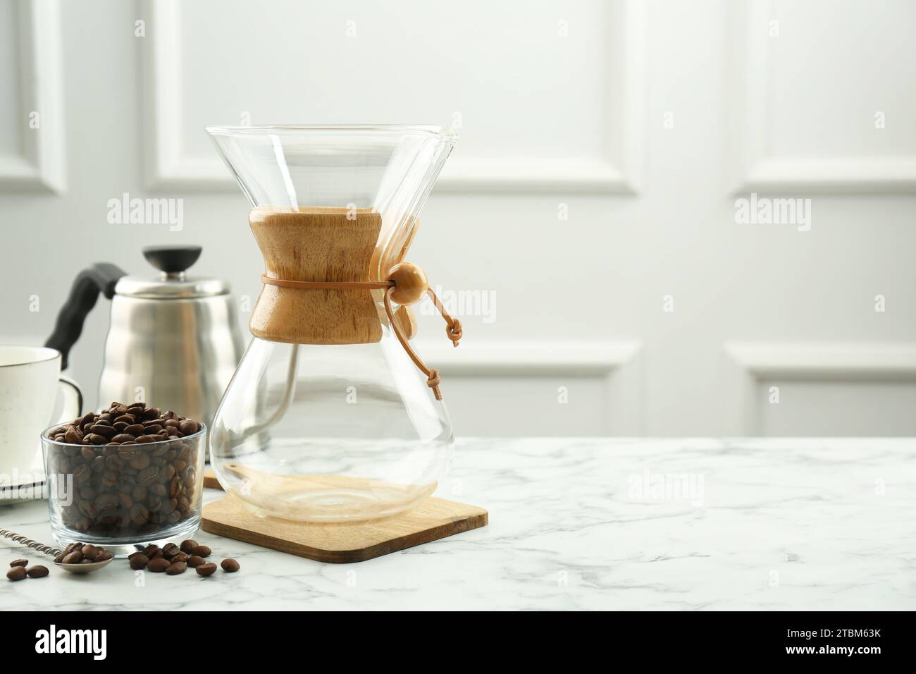 Glass chemex coffeemaker, kettle and beans on white marble table, space ...