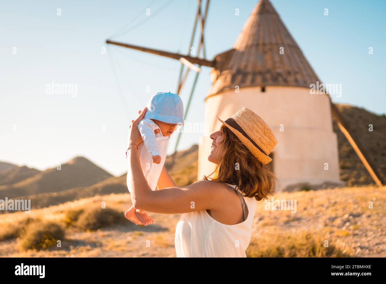 Mother raising a baby in arms next to a windmill in Cabo de Gata, Spain ...