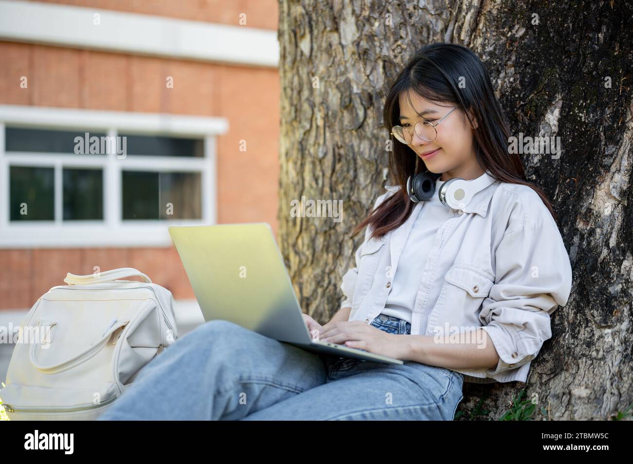 A charming and positive Asian female student is using her laptop ...