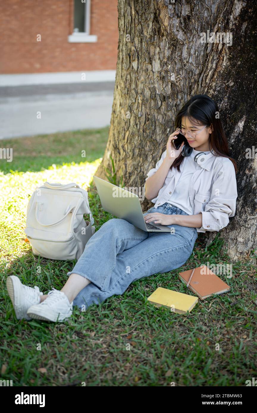 A beautiful young Asian female college student is talking on the phone ...