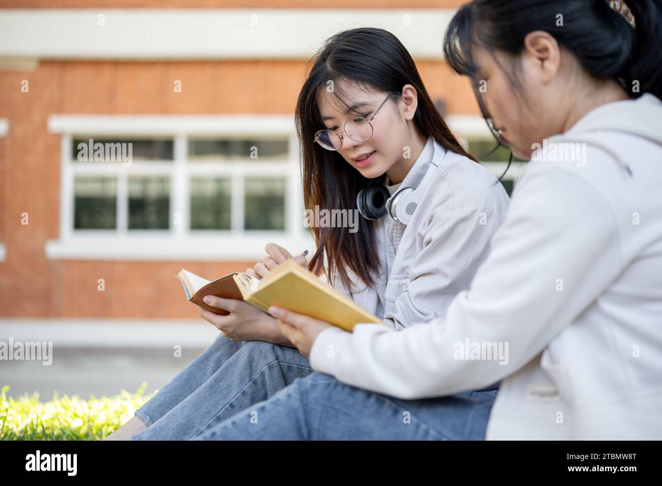 A happy and friendly young Asian female student is reading a book with ...