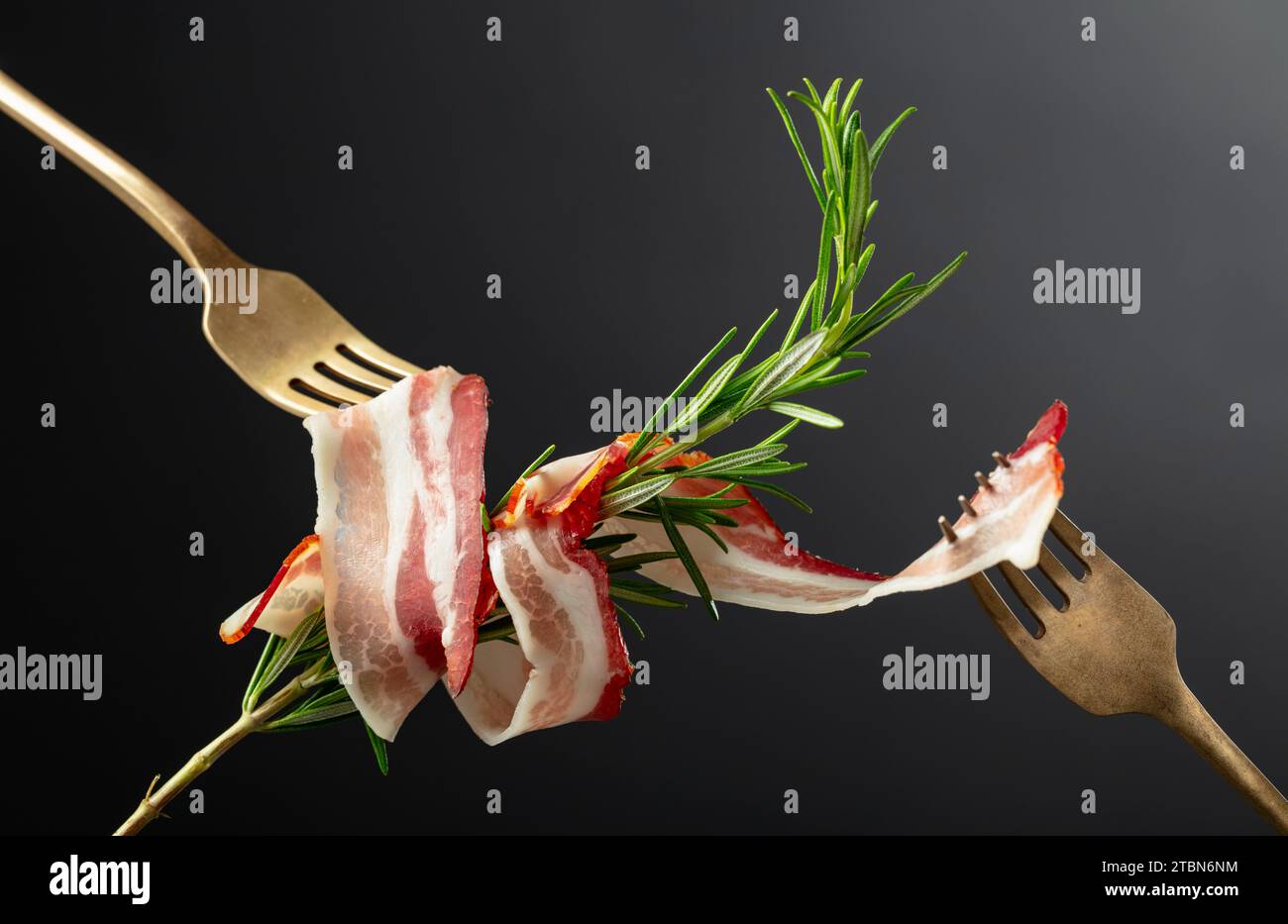 Dry-cured pork belly bacon with rosemary on a black background. Sliced ...