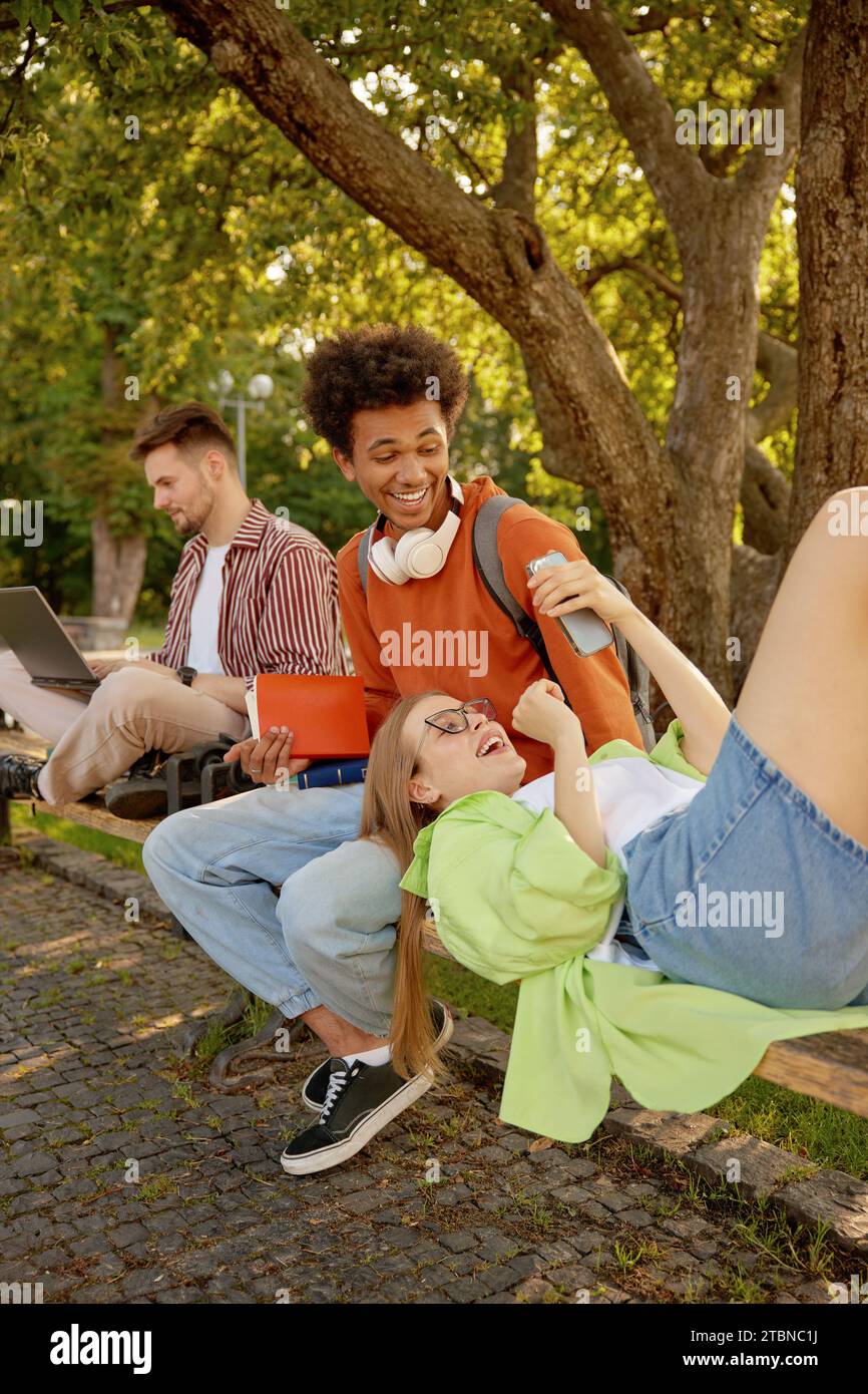 Multiracial students communicating while sitting together on park bench ...