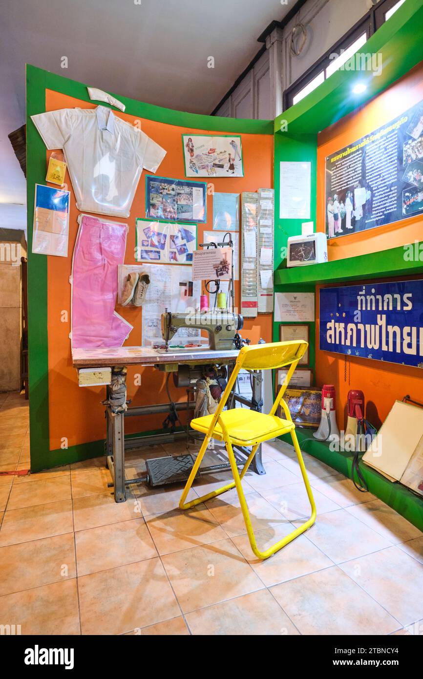 A sewing machine table with finished shirt, pants on the wall. In a ...