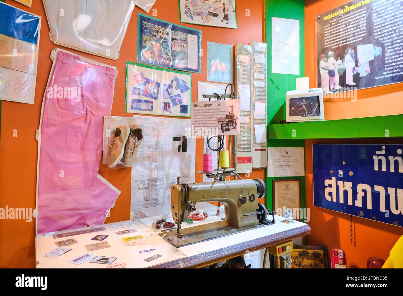 A sewing machine table with finished shirt, pants on the wall. In a ...