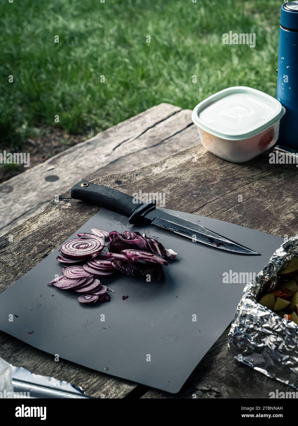Cutting board on an outdoor wooden camping table with cut red onion ...