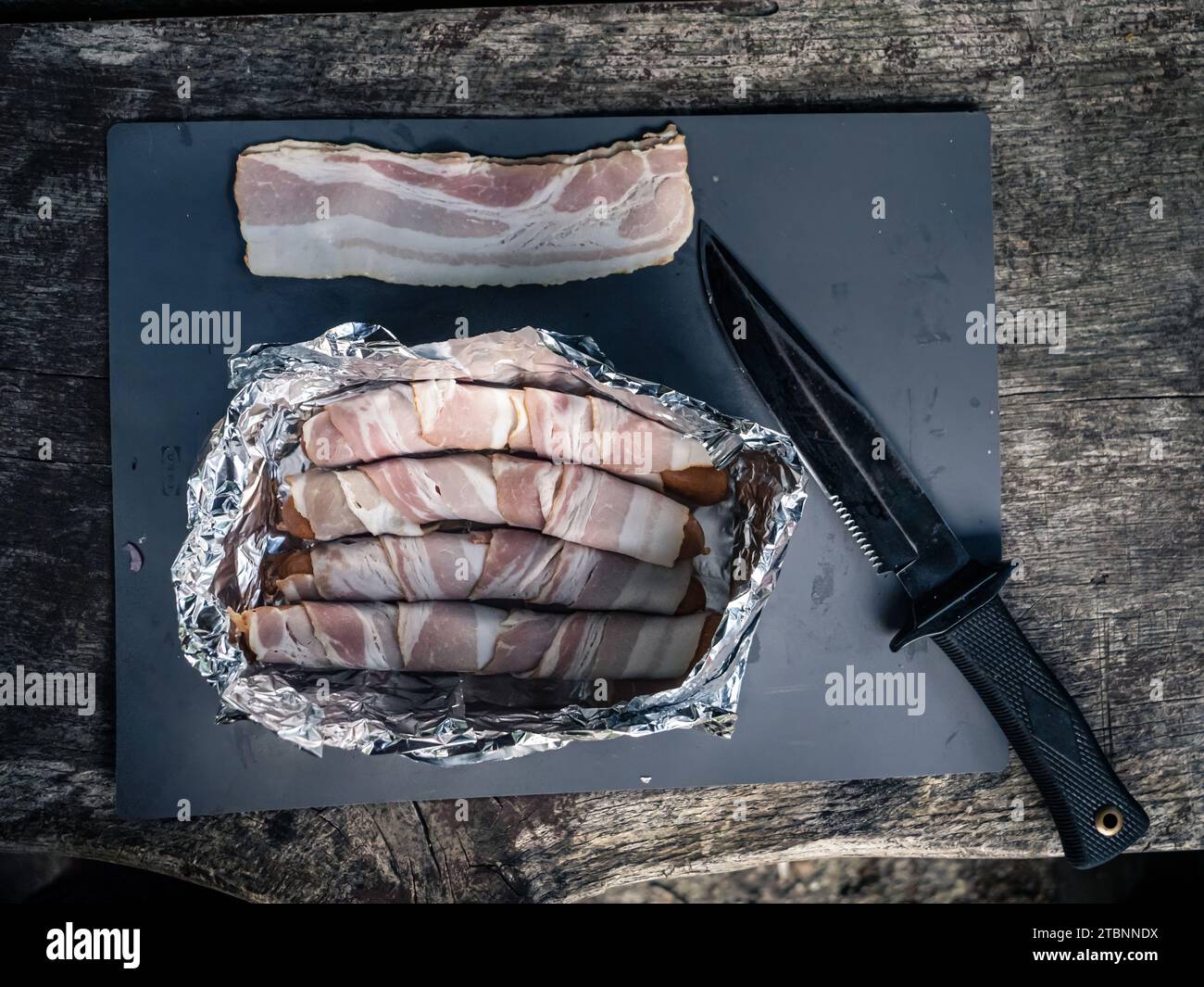 Flat lay of bacon wrapped sausages hot dogs in tin foil and a hunting ...