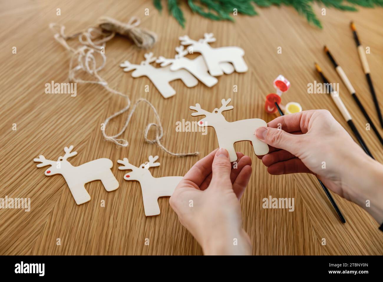 Hands crafting wooden reindeer ornaments on a table with paintbrushes ...