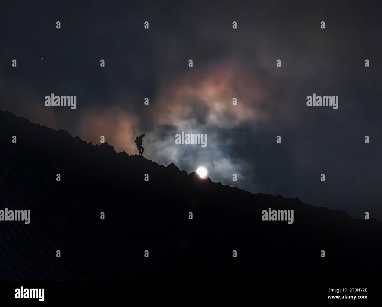 Man walks along mountain ridge at night with full moon and clouds Stock ...
