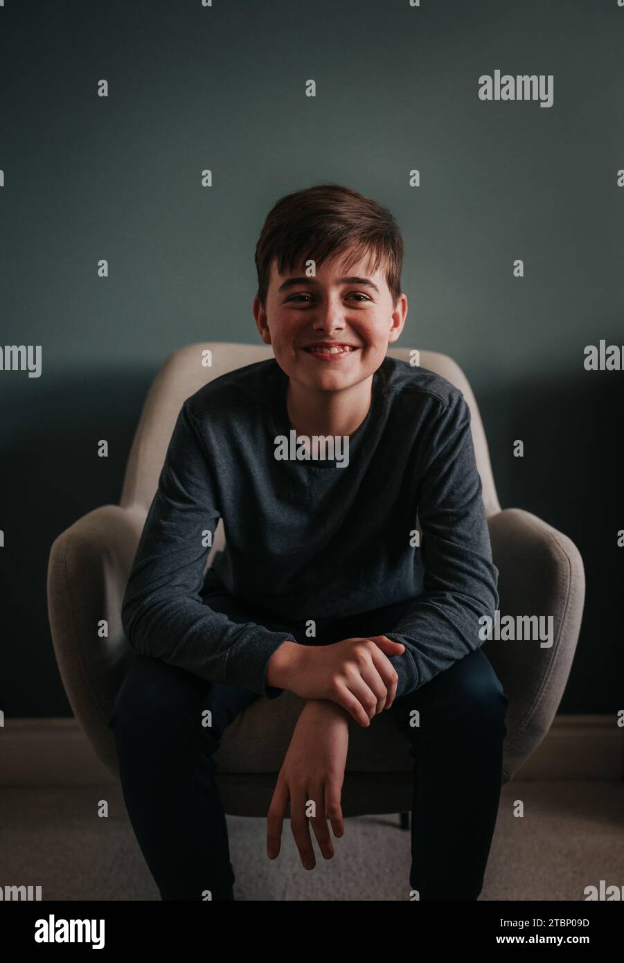 Portrait of happy boy sitting in chair indoors against blue wall Stock ...