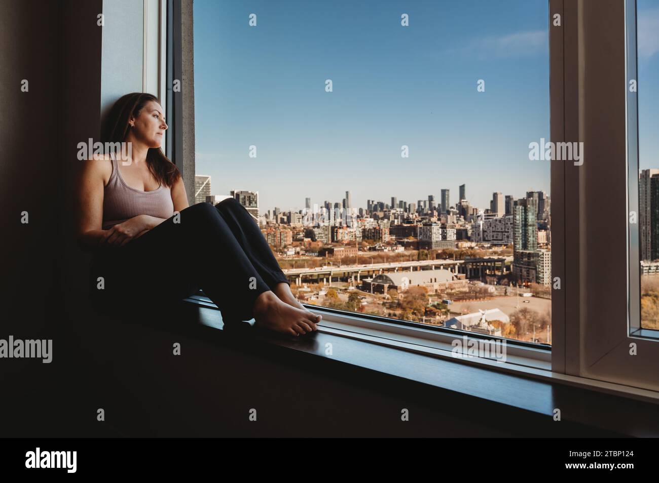 Woman sitting on sill of large window looking out at big city Stock ...