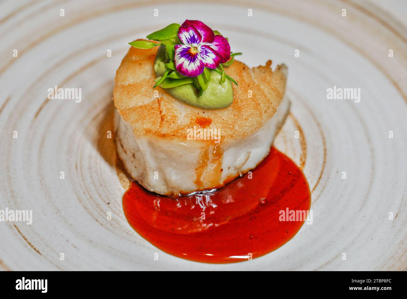 Gourmet dish with pan-seared fish, avocado puree, and vibrant flower ...