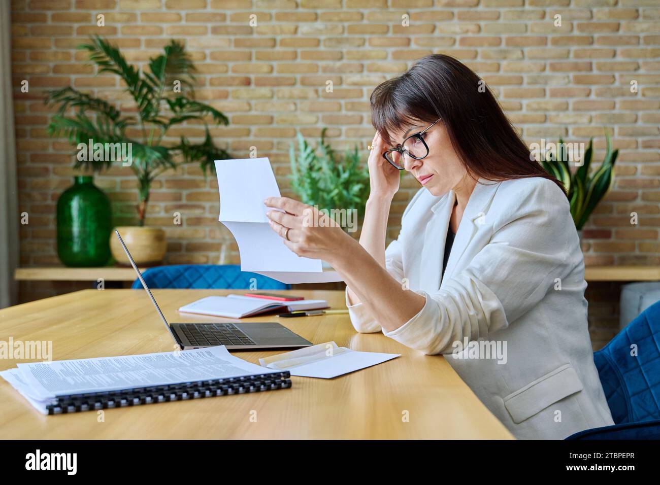 Serious mature businesswoman reading official letter, sitting in office ...