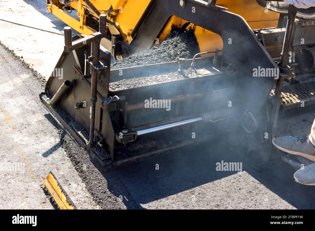 Pavement machine lays fresh bitumen asphalt on top of gravel base ...