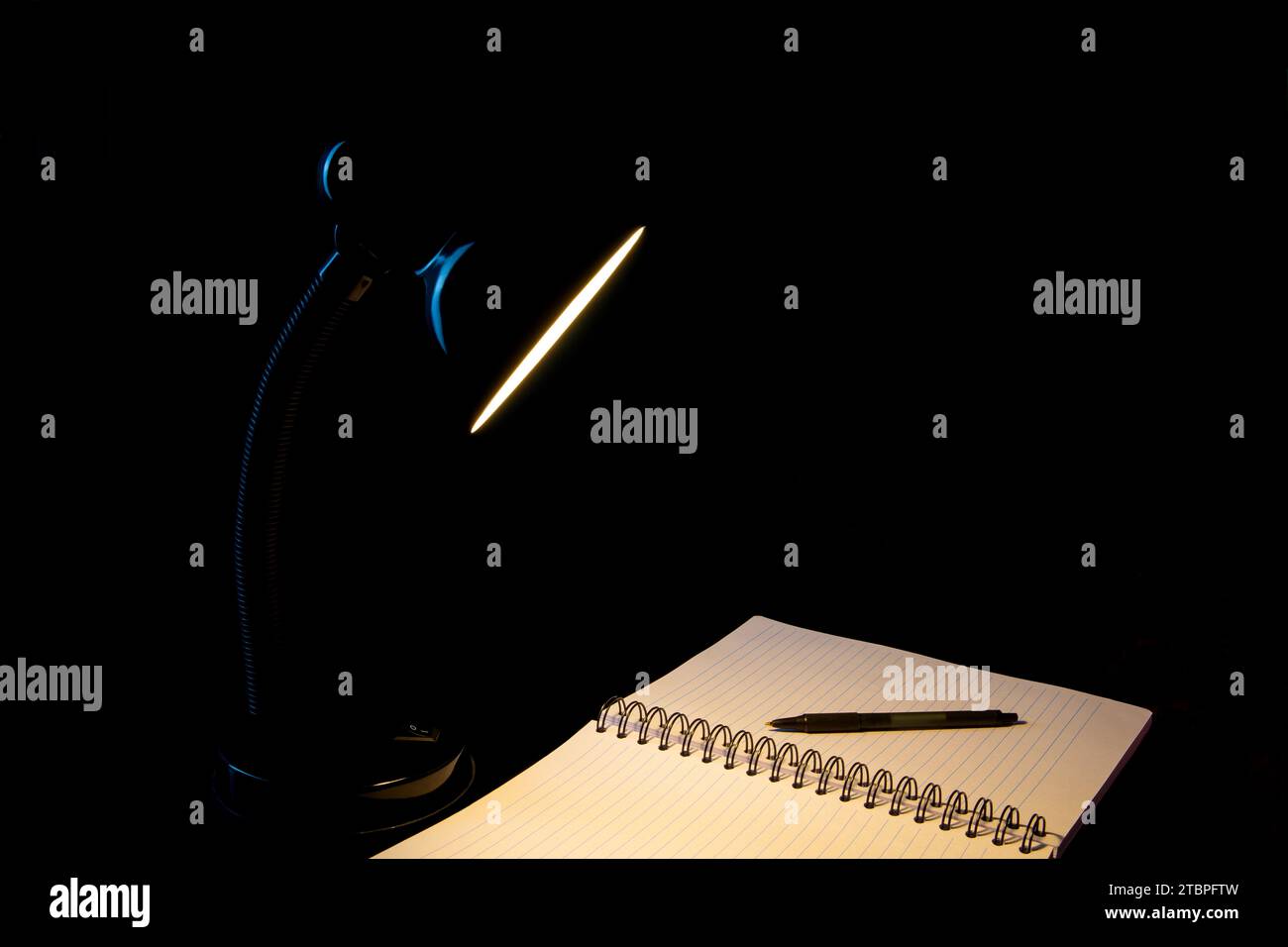 Closeup of a black desk lamp illuminating an open lined notepad and ...
