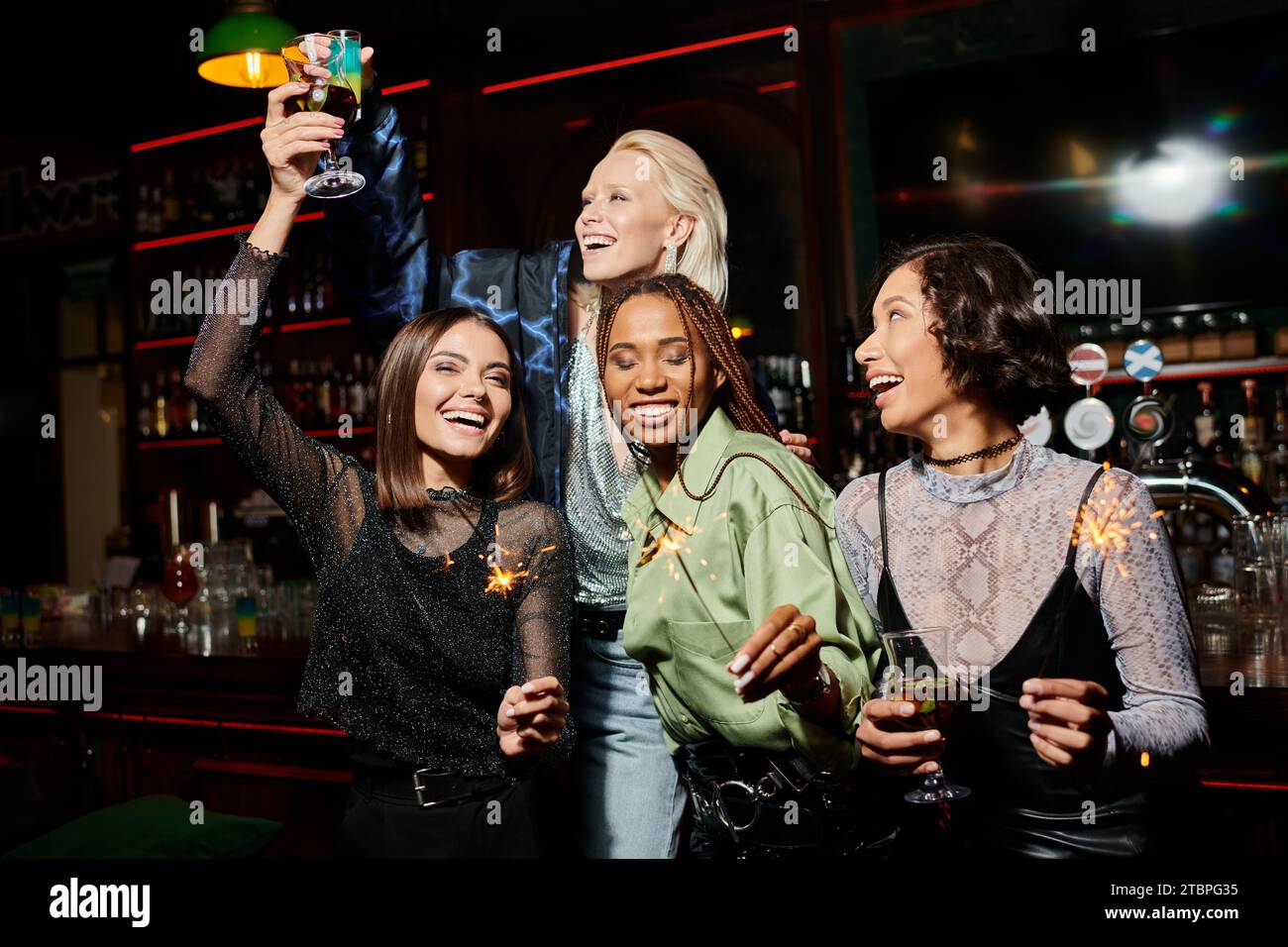 excited multicultural girlfriends toasting with cocktails and holding ...