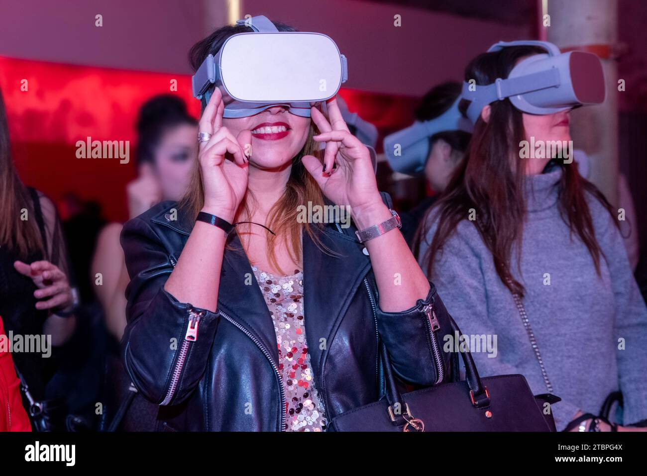 In a sea of red-lit anticipation, two women with VR glasses share smiles, surrounded by a ...
