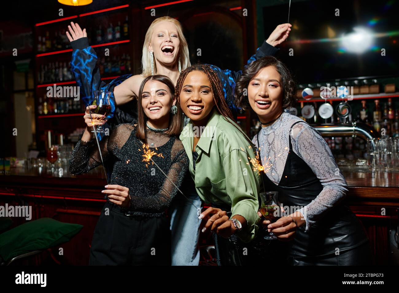 joyful multiethnic girlfriends with cocktails and festive sparklers ...