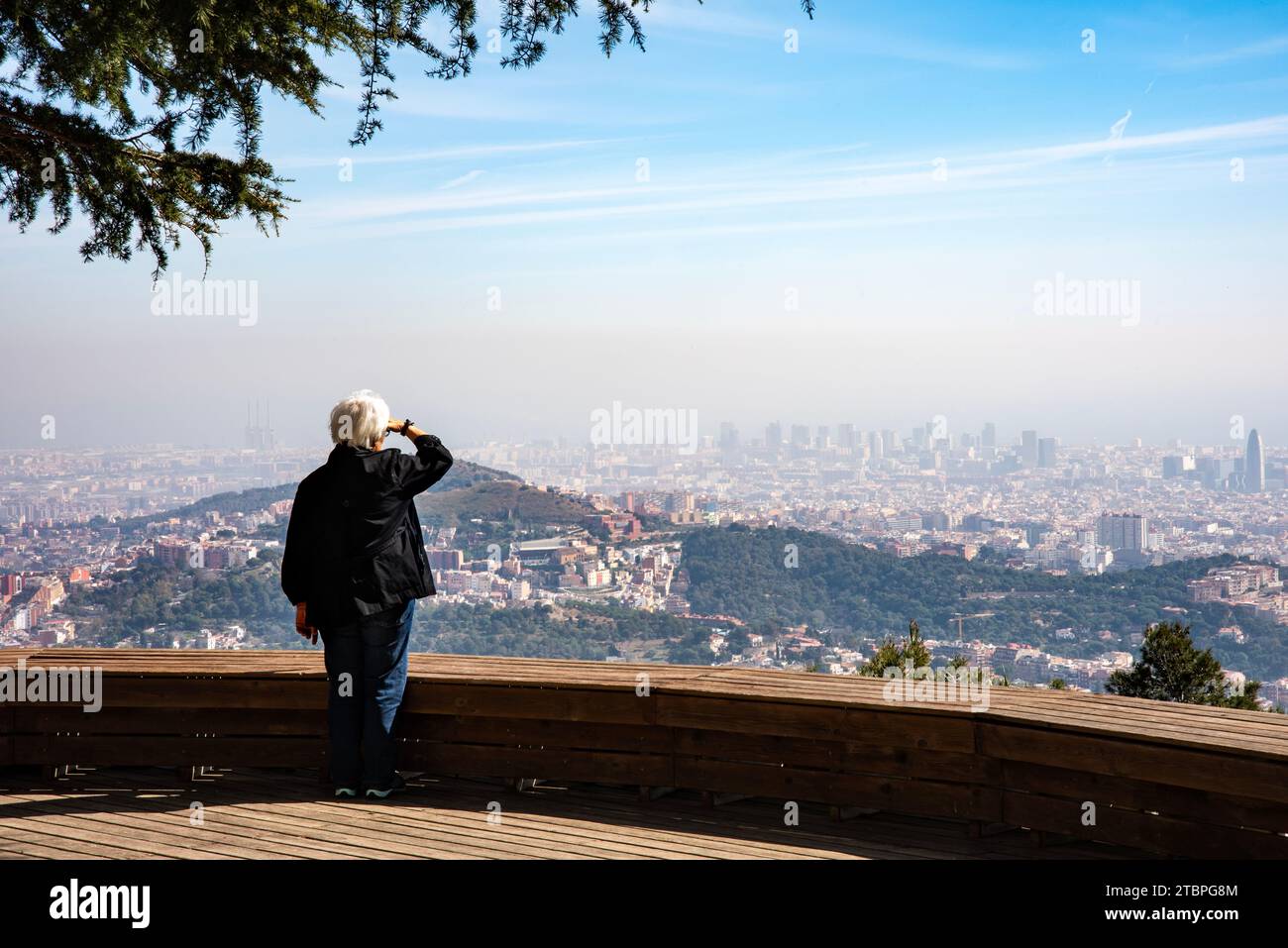 A venerable woman, hand shading the sun, gazes over Barcelona's ...