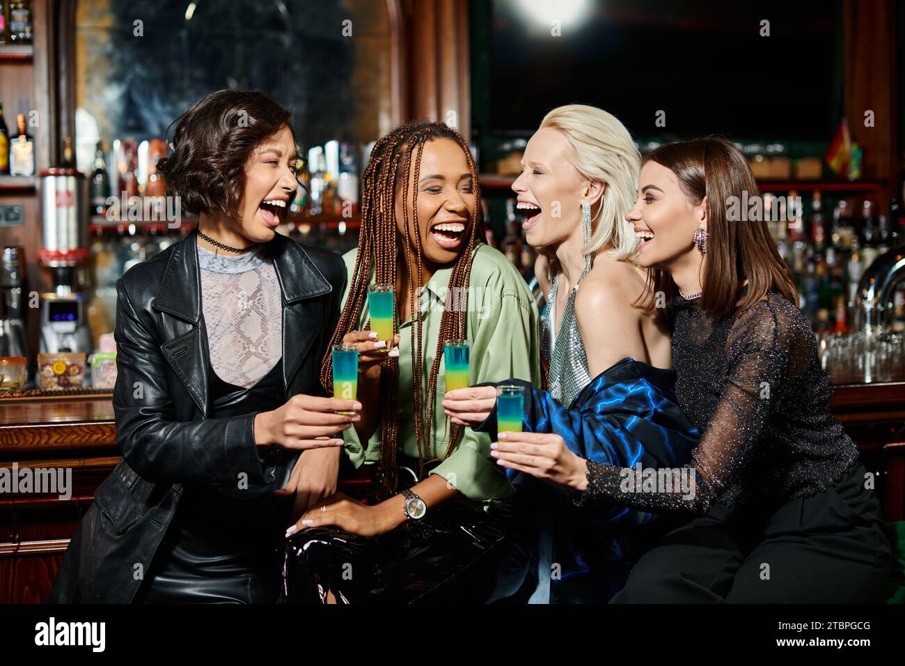 excited multiracial female friends with shot glasses laughing in modern ...