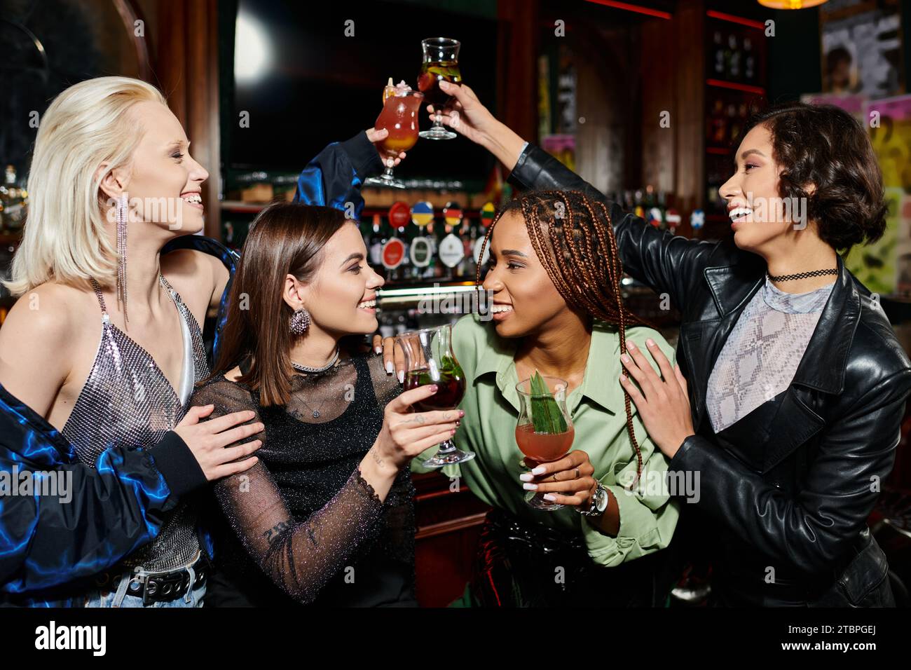 excited multiracial female friends clinking cocktail glasses while ...