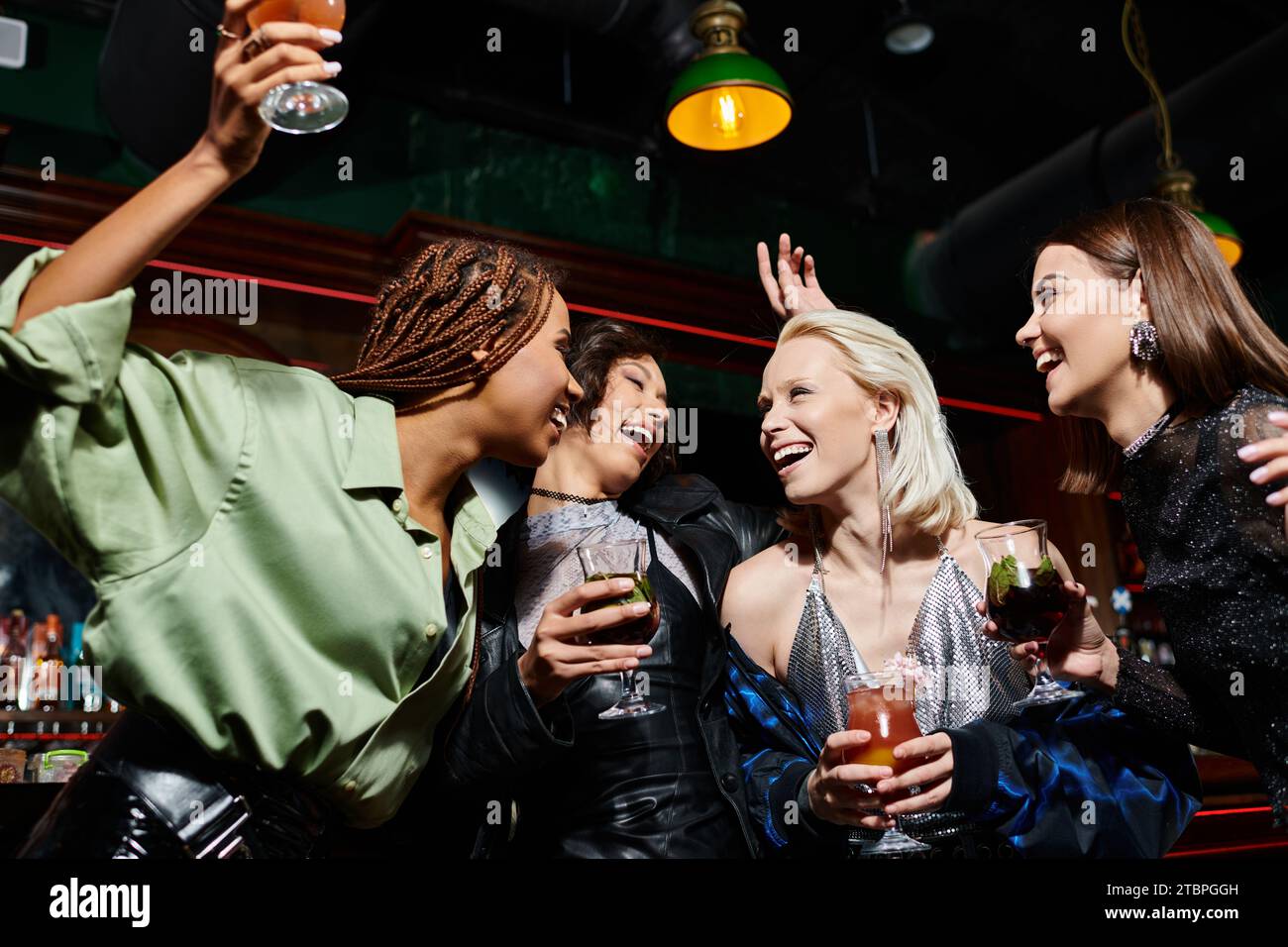 cheerful and stylish multicultural girlfriends with cocktails glasses ...