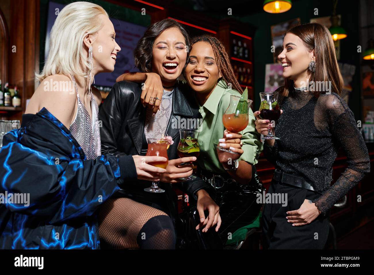 joyful multiethnic girlfriends with cocktail glasses embracing and ...