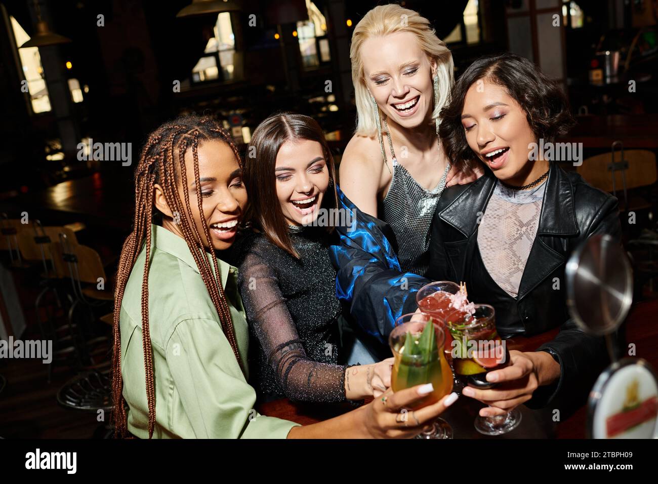 excited and young multicultural women clinking delicious cocktails in ...