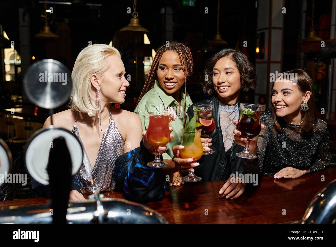 carefree multicultural girlfriends toasting with cocktails in vibrant ...