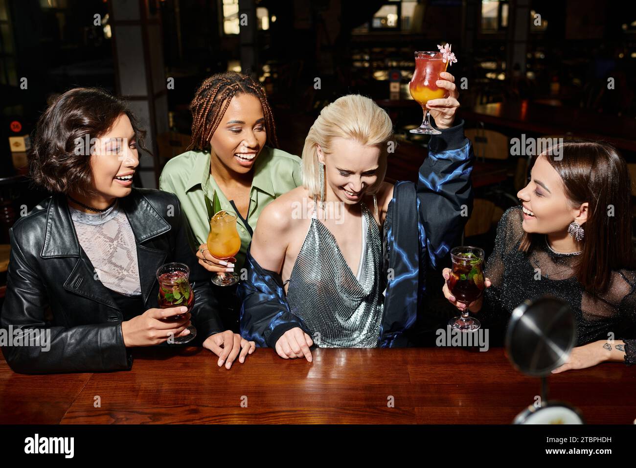 excited blonde woman toasting with cocktail glass near elegant ...