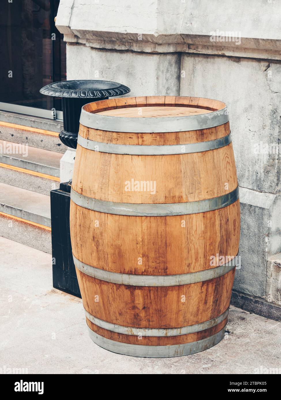 A large wooden barrel sits on a cobblestone sidewalk beside a set of ...