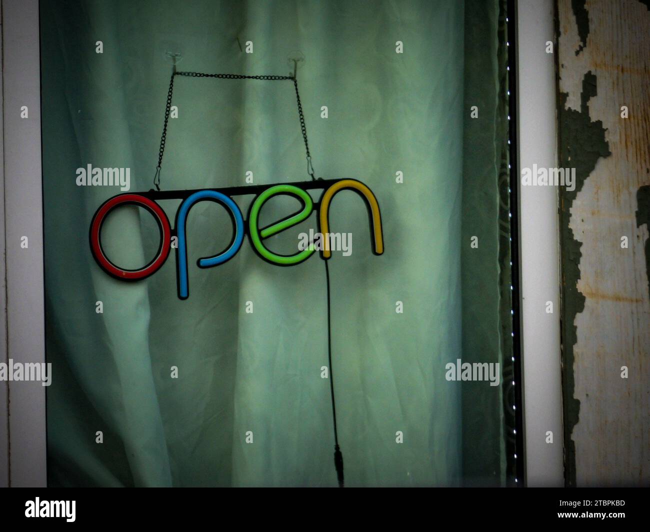 An illuminated open sign hangs from a white wall with green curtains ...