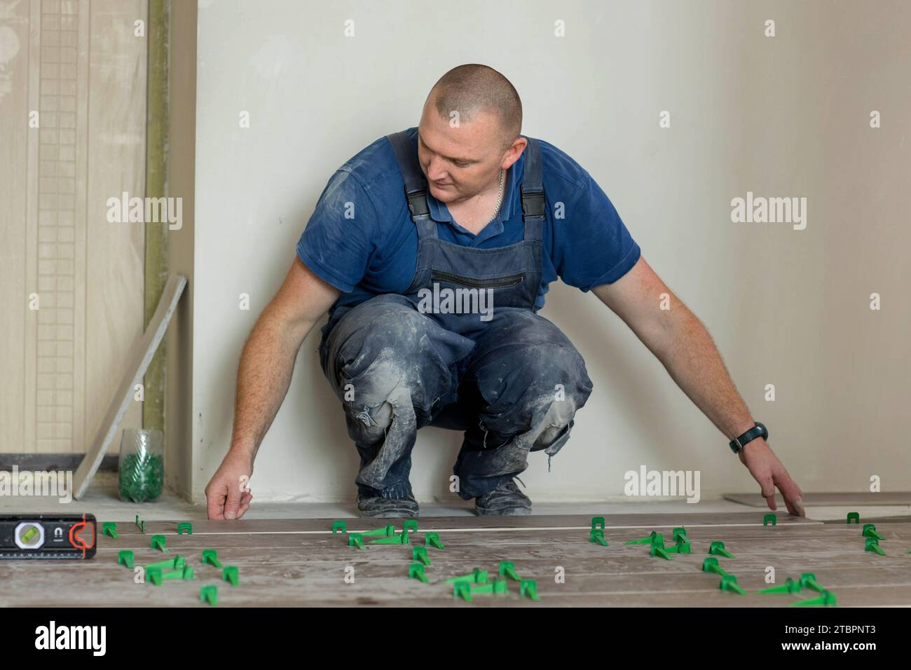 Tiler placing ceramic wall tile in position over adhesive with lash ...