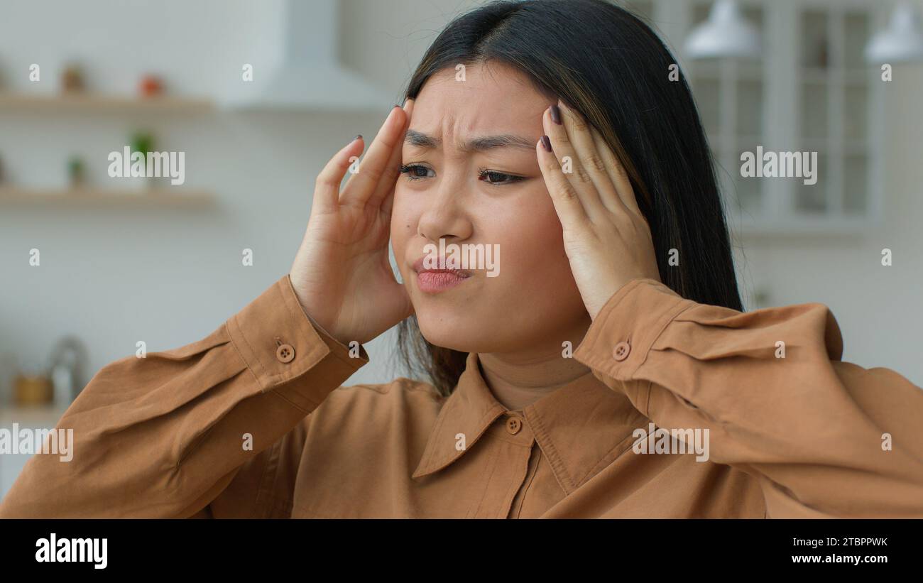 Tired sick Asian woman feel headache pain massaging temples touch aching head hurt grimace ...